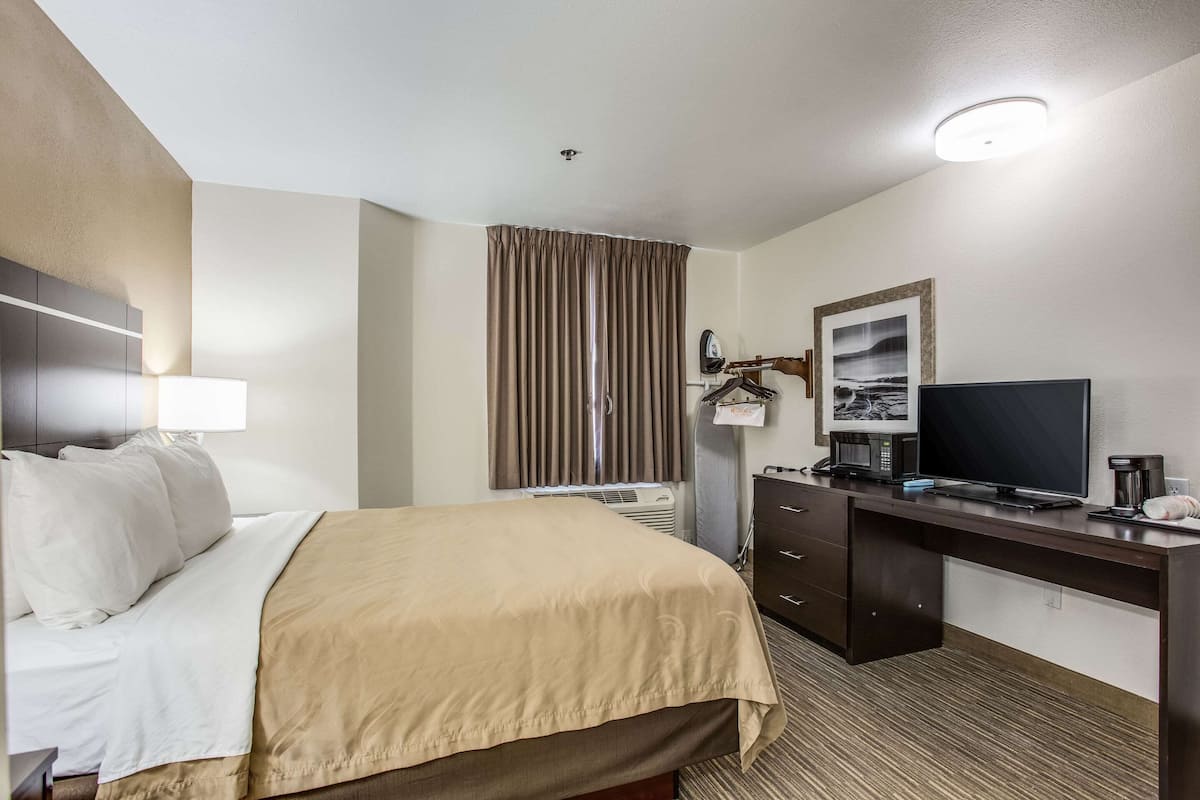 Quarto de hotel com uma cama, uma escrivaninha com televisão, uma cafeteira e um porta-retrato na parede.