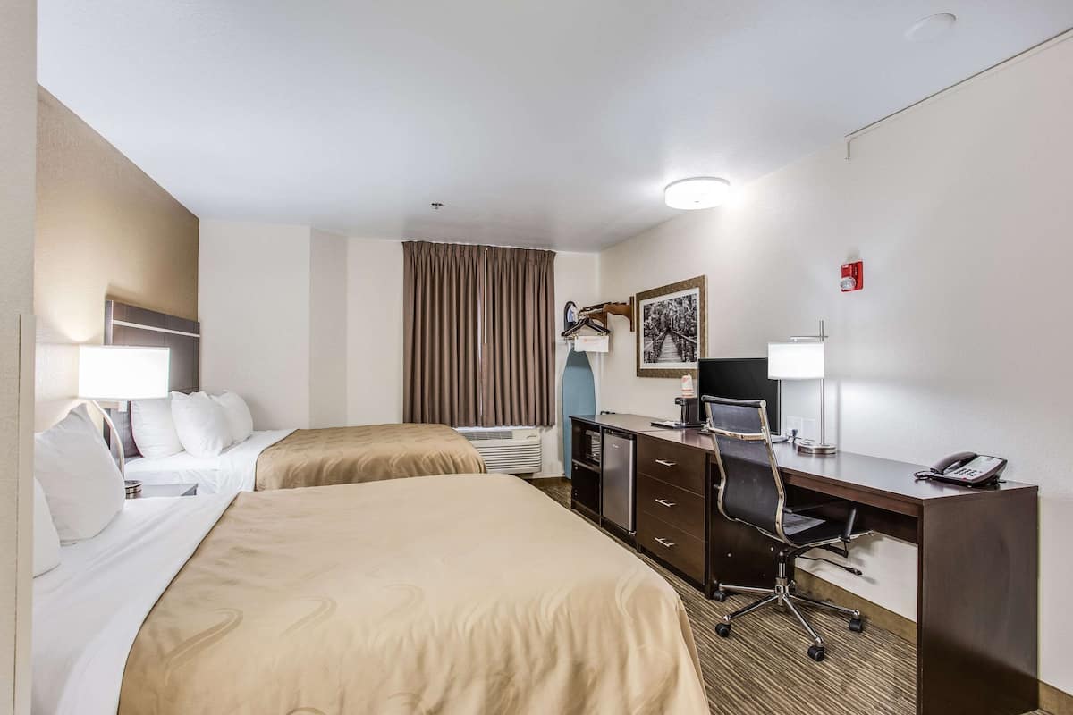 Quarto de hotel com duas camas, uma escrivaninha com computador, telefone e guarda-roupa.