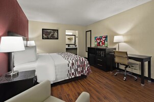 Quarto de hotel com cama, escrivaninha, cadeira e televisão.