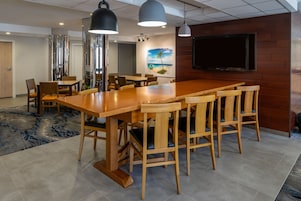 Sala de conferência com uma grande mesa de madeira, várias cadeiras e iluminação pendente.