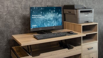 Uma mesa de escritório moderna com monitor de computador, teclado, rato e uma impressora Brother.