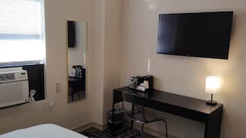 Quarto de hotel com cama, escrivaninha com cadeira, televisão de tela plana, espelho, cafeteira e luminária.