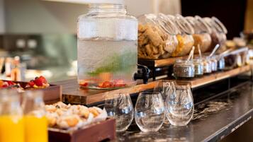 Disposição de buffet com um grande dispensador de água, diversos alimentos e copos vazios em um balcão.