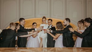 Um grupo de pessoas brindando com taças de champanhe em uma sala com mesa de mármore e painéis de parede ornamentados.