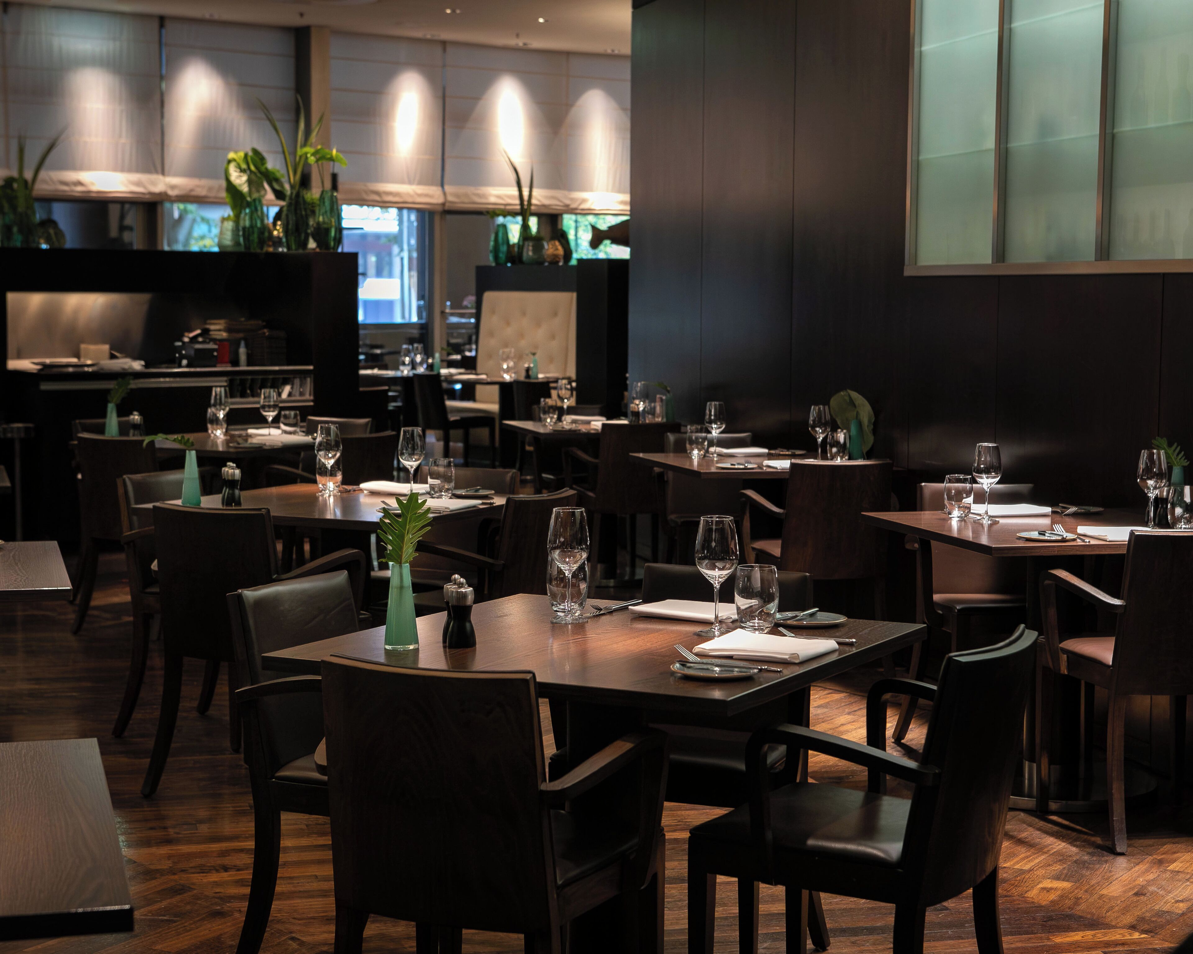 Interior moderno de restaurante com várias mesas e cadeiras, completo com copos de vinho e talheres.