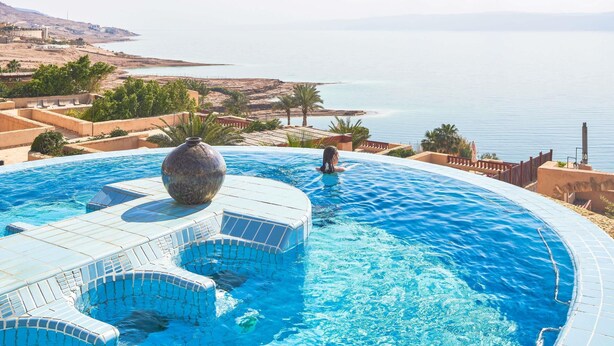 Piscina com vista para o mar, um vaso grande e uma pessoa a nadar.