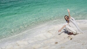 Uma pessoa sentada na praia, com águas turquesa cristalinas e areal arenoso.