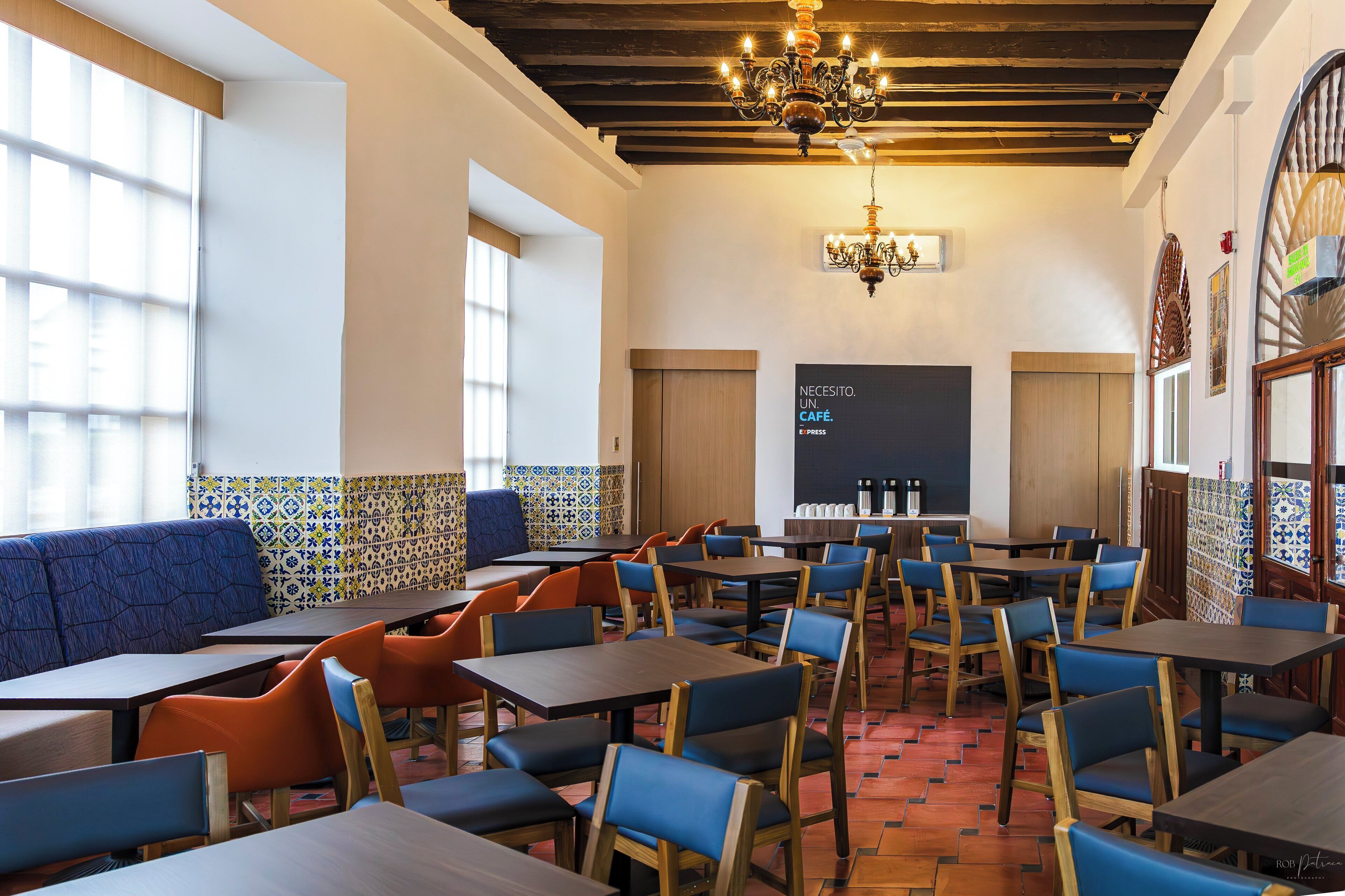 Interior de restaurante com mesas e cadeiras altas, parede estampada e lustre.
