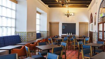 Interior de restaurante com mesas e cadeiras altas, parede estampada e lustre.