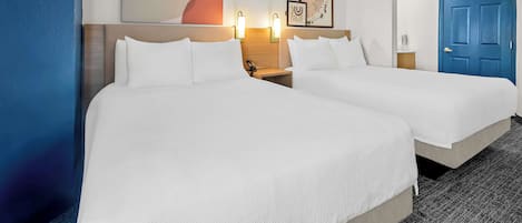 Quarto de hotel com duas camas, porta azul e obras de arte nas paredes.