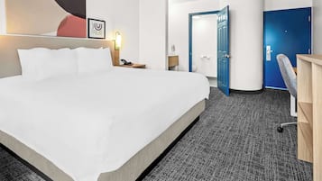 Quarto de hotel com cama grande, escrivaninha, cadeira, banheiro e porta azul.