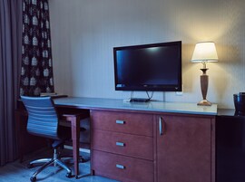 Quarto de hotel com televisão de tela plana, escrivaninha com luminária, uma cadeira e armário.