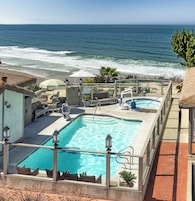 Uma área de piscina com vista para o oceano, cadeiras de descanso e um pequeno deque.