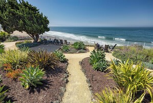 Um jardim costeiro com um caminho que leva a cadeiras de praia e vista para o oceano.
