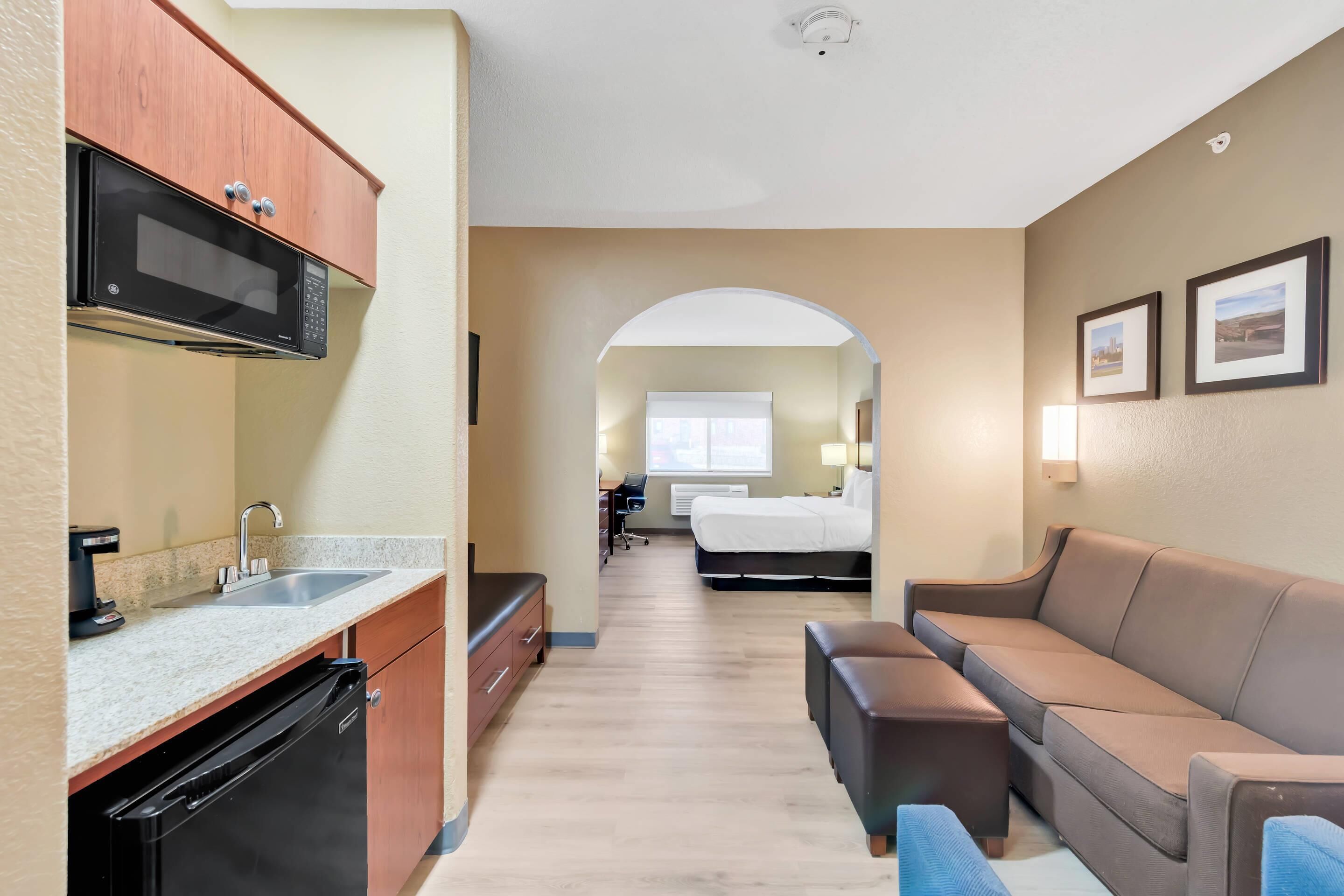 Quarto de hotel compacto com cozinha compacta, cama, sofá e pequena área de refeições.