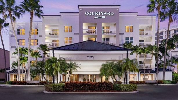 Um hotel Courtyard Marriott com fachada moderna, várias varandas e palmeiras.