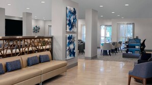 Um saguão de hotel moderno com um sofá bege, uma área de refeições e arte abstrata nas paredes.