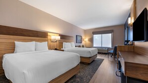 Quarto de hotel com duas camas, uma escrivaninha e uma janela grande.