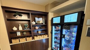 Um corredor com um armário de madeira exibindo objetos decorativos e uma máquina de venda automática de bebidas.