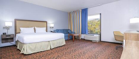 Quarto de hotel com cama, escrivaninha, cadeira e janela com cortinas.