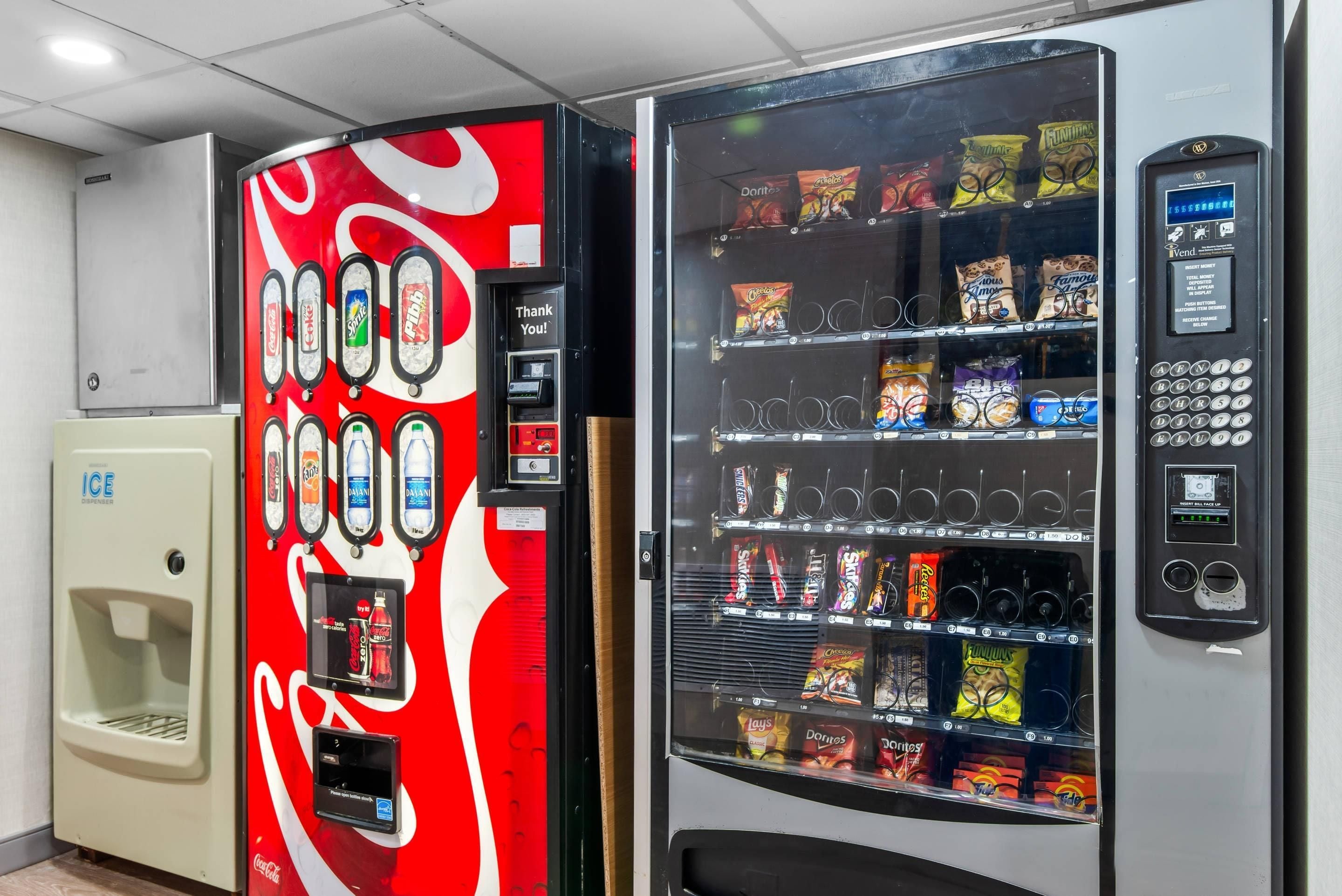 Máquina automática com logotipo da Coca-Cola, dispensador de bebidas e área de venda de lanches.