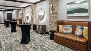 Um lobby de hotel com um sofá de couro marrom, mesas redondas, um balcão de recepção e uma parede de destaque em pedra.