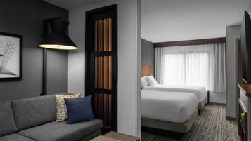 Quarto de hotel com sofá, duas camas, televisão e uma janela grande com cortinas.