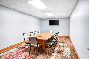 Sala de conferências com uma mesa comprida, cadeiras, uma TV de tela plana e um tapete estampado.