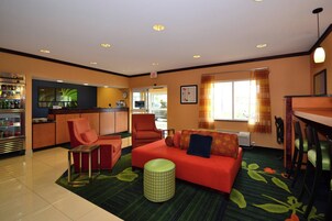 Quarto de hotel com sofá vermelho, uma pequena mesa, um banquinho verde, uma cozinha compacta e uma área de jantar com cadeiras.