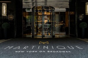 Entrada do Martinique New York on Broadway, com porta giratória, portas de vidro e placa com o nome do hotel.