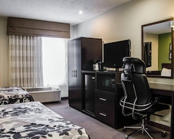 Quarto de hotel com cama, escrivaninha com computador, cadeira, espelho e janela com cortinas.