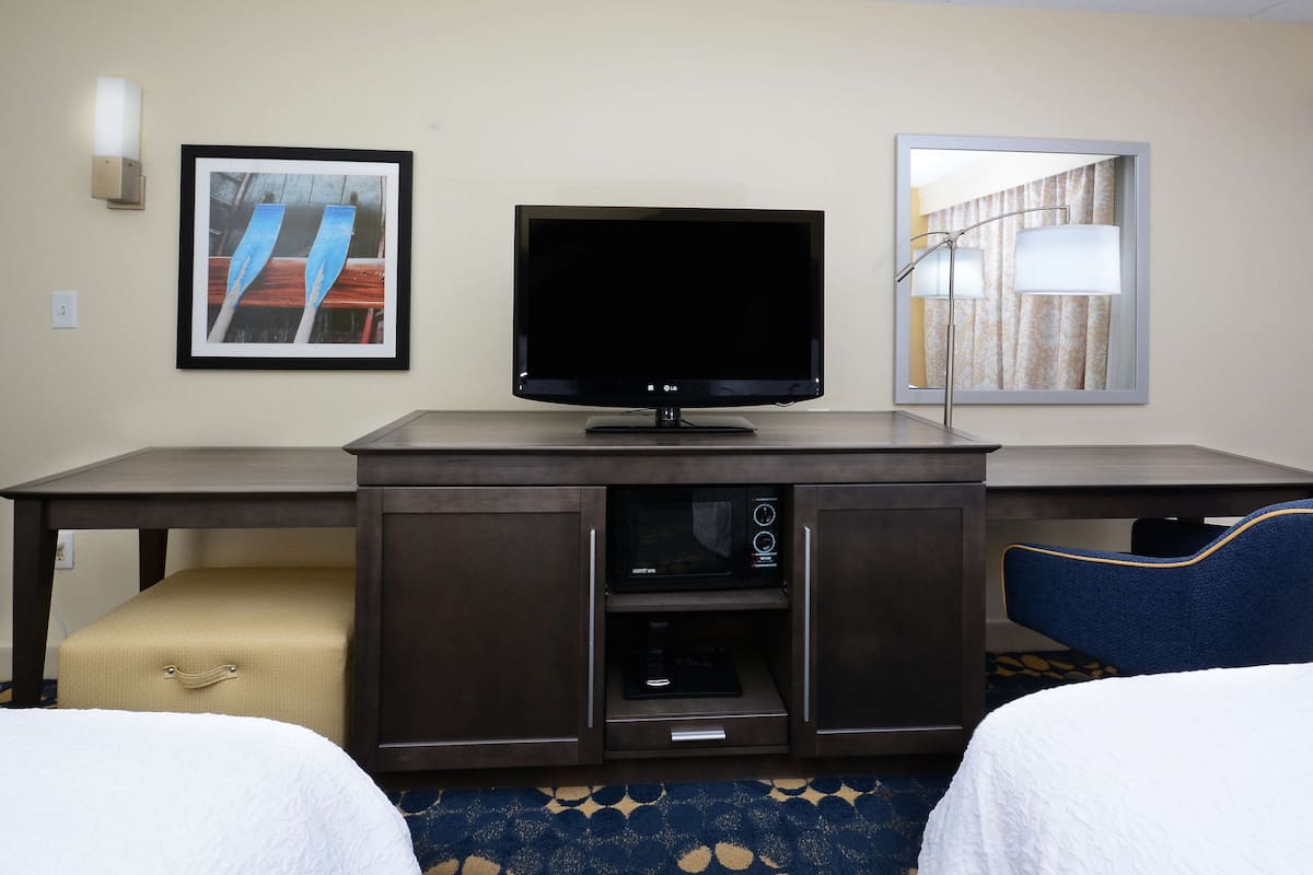 Quarto de hotel com televisão de tela plana, micro-ondas, armário pequeno, cama e uma cadeira.