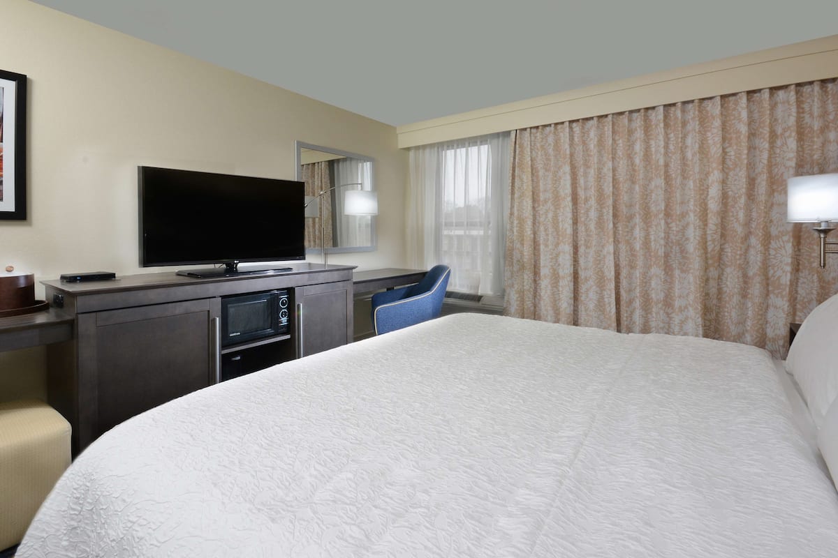 Quarto de hotel com uma cama grande, uma escrivaninha, uma televisão de tela plana, micro-ondas e uma cadeira.