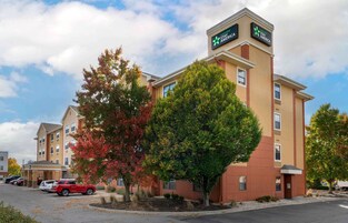 Um hotel Stay America com fachada bege, várias janelas e um estacionamento com carros.