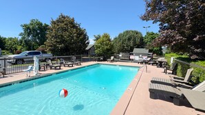 Piscina com espreguiçadeiras e uma bola de praia, cercada por árvores e um muro.