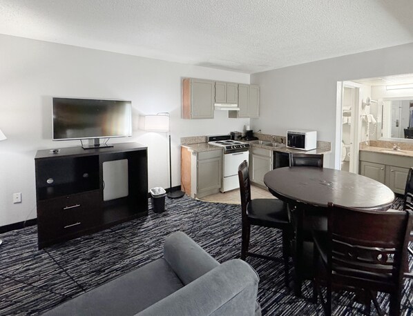 Quarto de hotel compacto com cozinha compacta, área de refeições, sofá e TV.