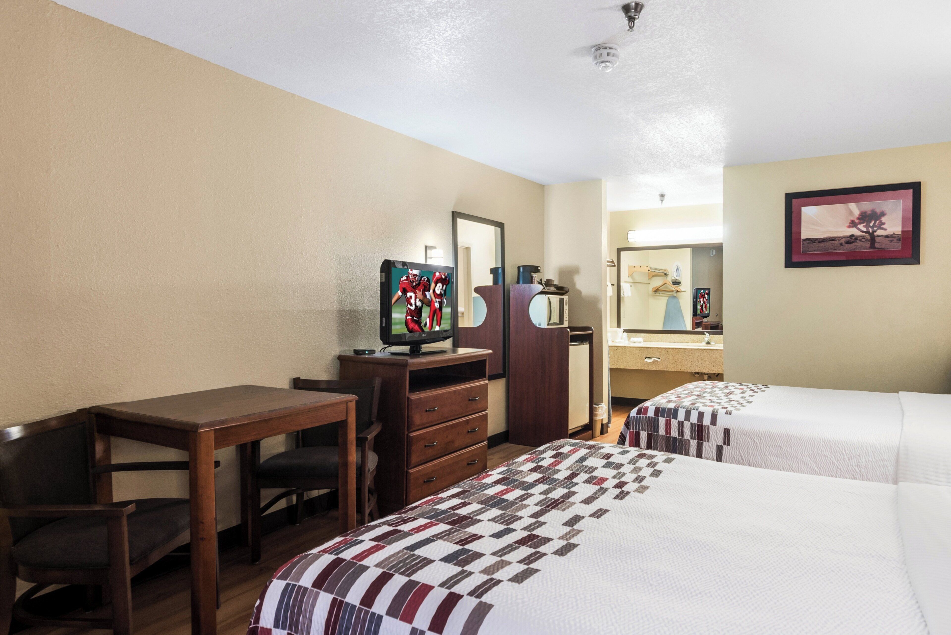 Quarto de hotel com duas camas, uma escrivaninha, televisão, cómoda e espelho.