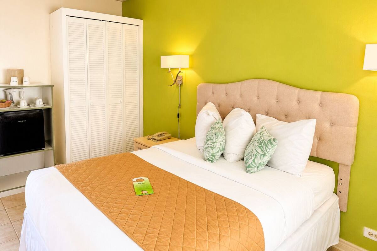 Quarto de hotel com cama, mesa de cabeceira com telefone, guarda-roupa e cozinha compacta.