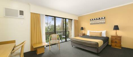 Quarto de hotel com cama, escrivaninha, cadeira, mesa pequena, varanda com cortinas e ventilador de teto.