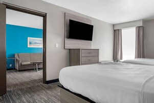Quarto de hotel com uma cama grande, televisão de tela plana na parede, sofá e uma mesa pequena.