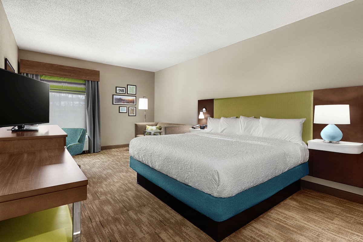 Quarto de hotel com uma cama grande, uma escrivaninha, uma TV e uma janela com cortinas.