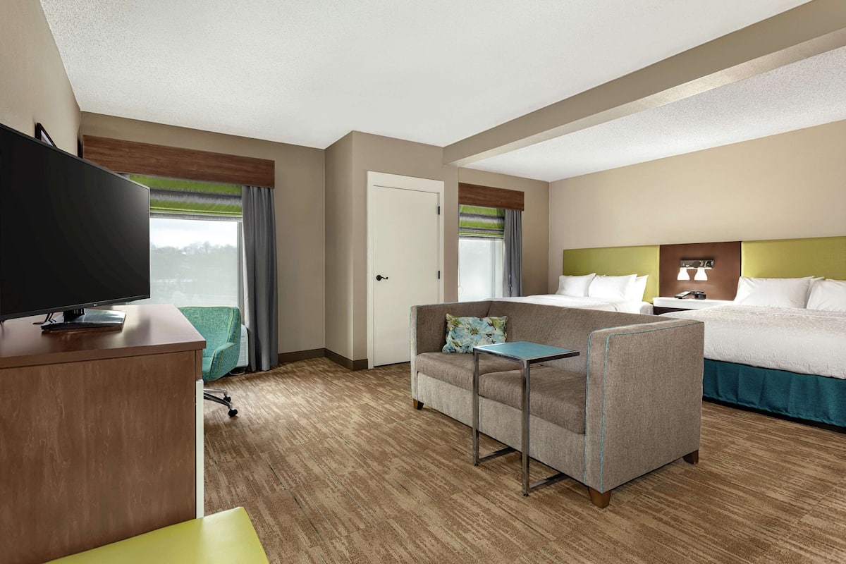 Quarto de hotel com cama, sofá, televisão e escrivaninha.