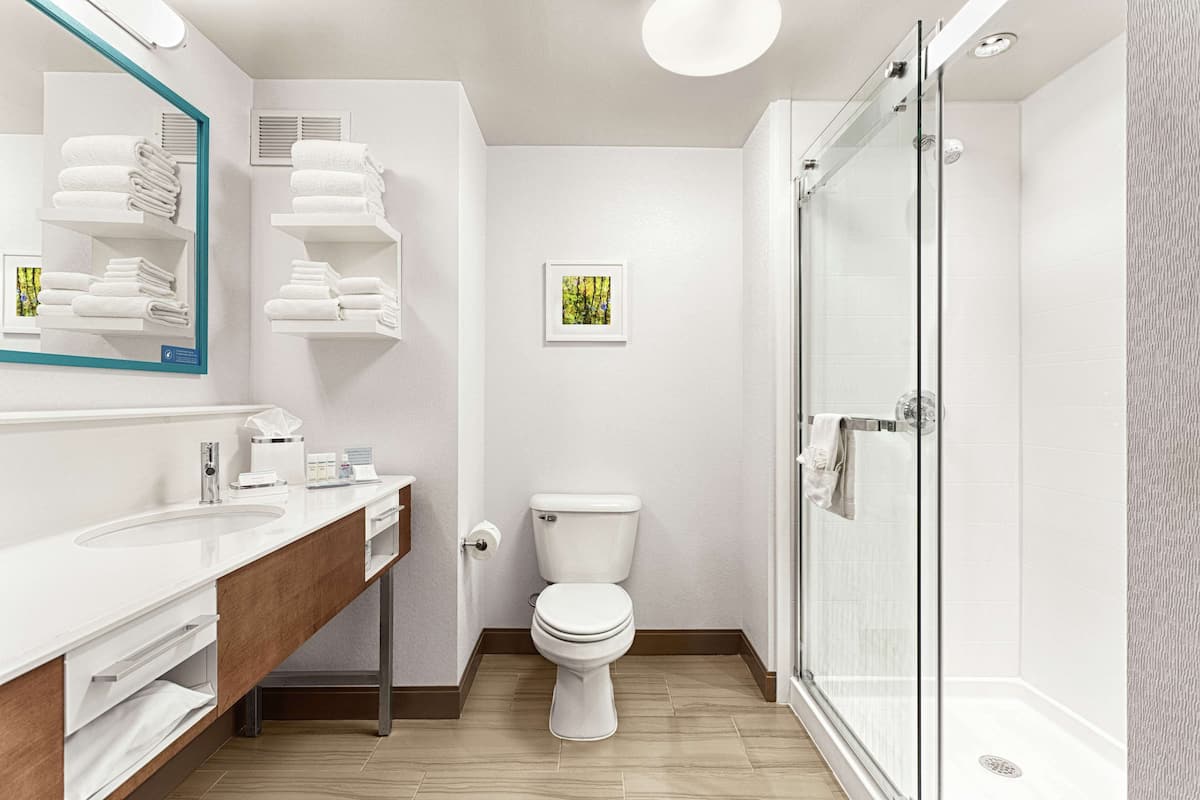 Uma casa de banho moderna com lavatório branco, espelho e sanita, cabine de duche em vidro e barra de toalhas.
