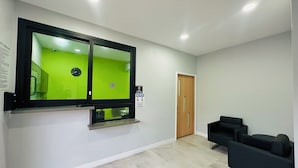 Uma área de recepção com parede verde, um relógio, um aviso de 'Não Aceitamos Animais' e uma porta.