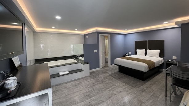 Quarto de hotel moderno com uma cama grande, banheiro separado com banheira, escrivaninha com cadeira e televisão de tela plana.