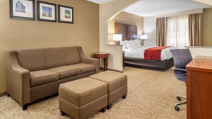 Quarto de hotel com sofá, banquinho, cama, escrivaninha e quadros na parede.