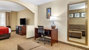 Quarto de hotel com cama, escrivaninha, cadeira, luminária, televisão e um espelho grande.