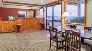 Quarto de hotel com uma receção de madeira, uma mesa de jantar com cadeiras e grandes janelas com vista para o exterior.