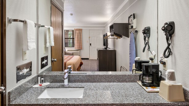 Casa de banho de hotel com lavatório, espelho, porta-toalhas e máquina de café.