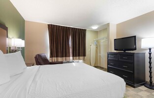 Quarto de hotel com uma cama grande, televisão, penteadeira, cadeira e chuveiro.